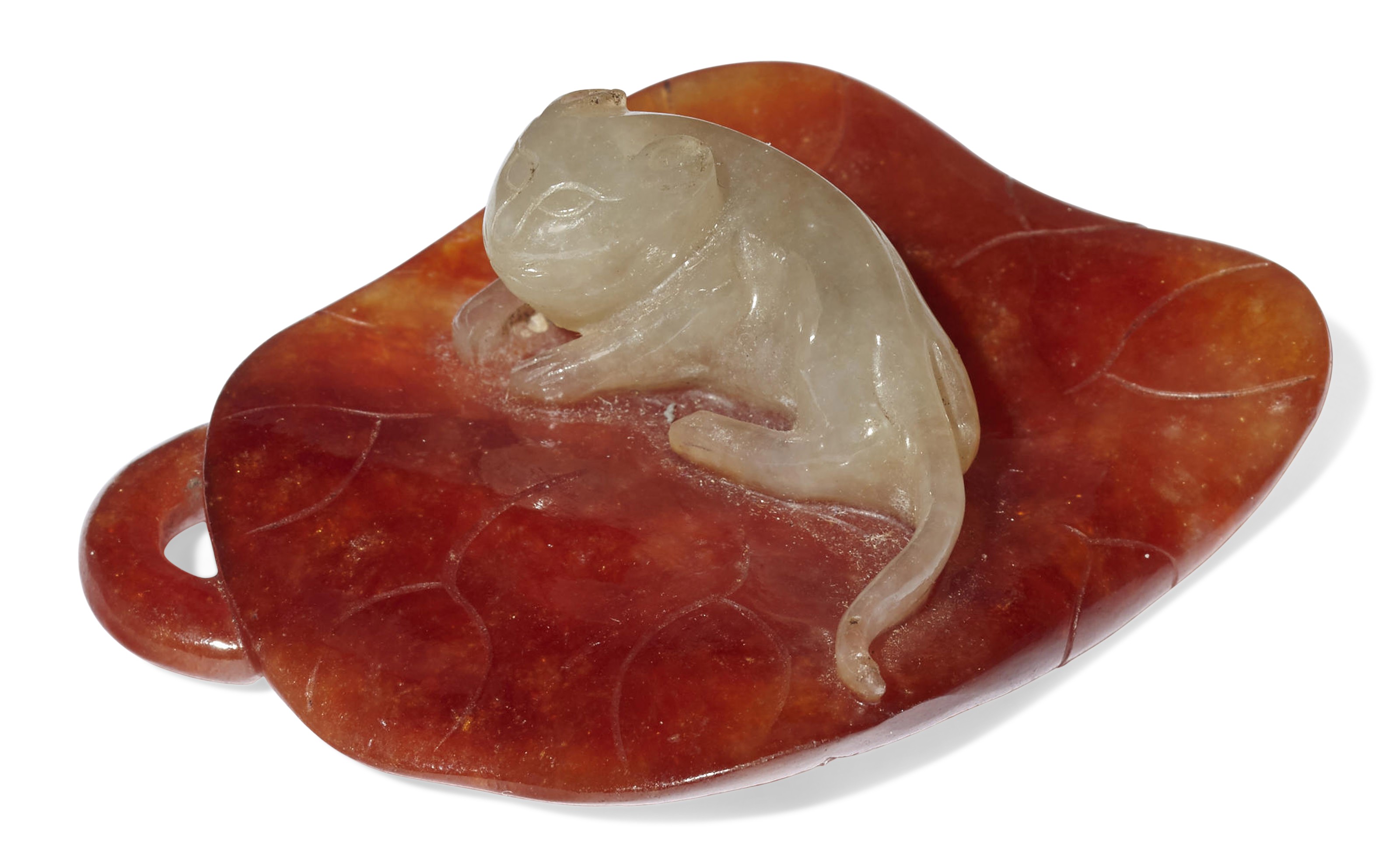 A WHITE AND REDDISH-BROWN JADEITE CARVING OF A CAT ON A LOTUS PAD ...