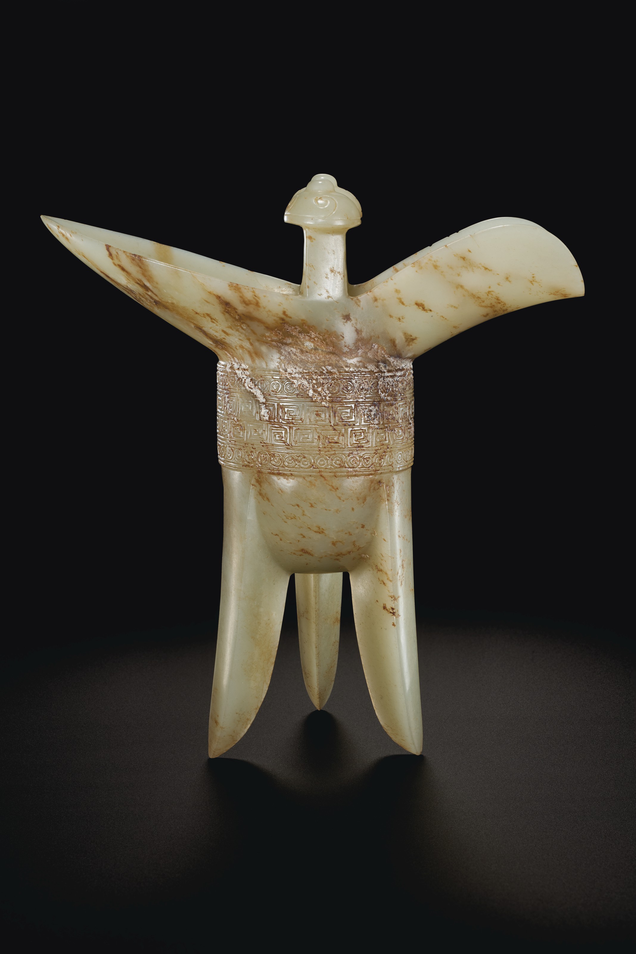 A RARE ARCHAISTIC PALE GREEN AND RUSSET JADE TRIPOD VESSEL, JUE