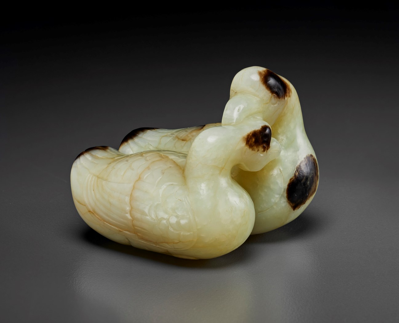 A PALE CELADON AND BLACKISH-BROWN JADE CARVING OF TWO RECUMBENT GEESE ...
