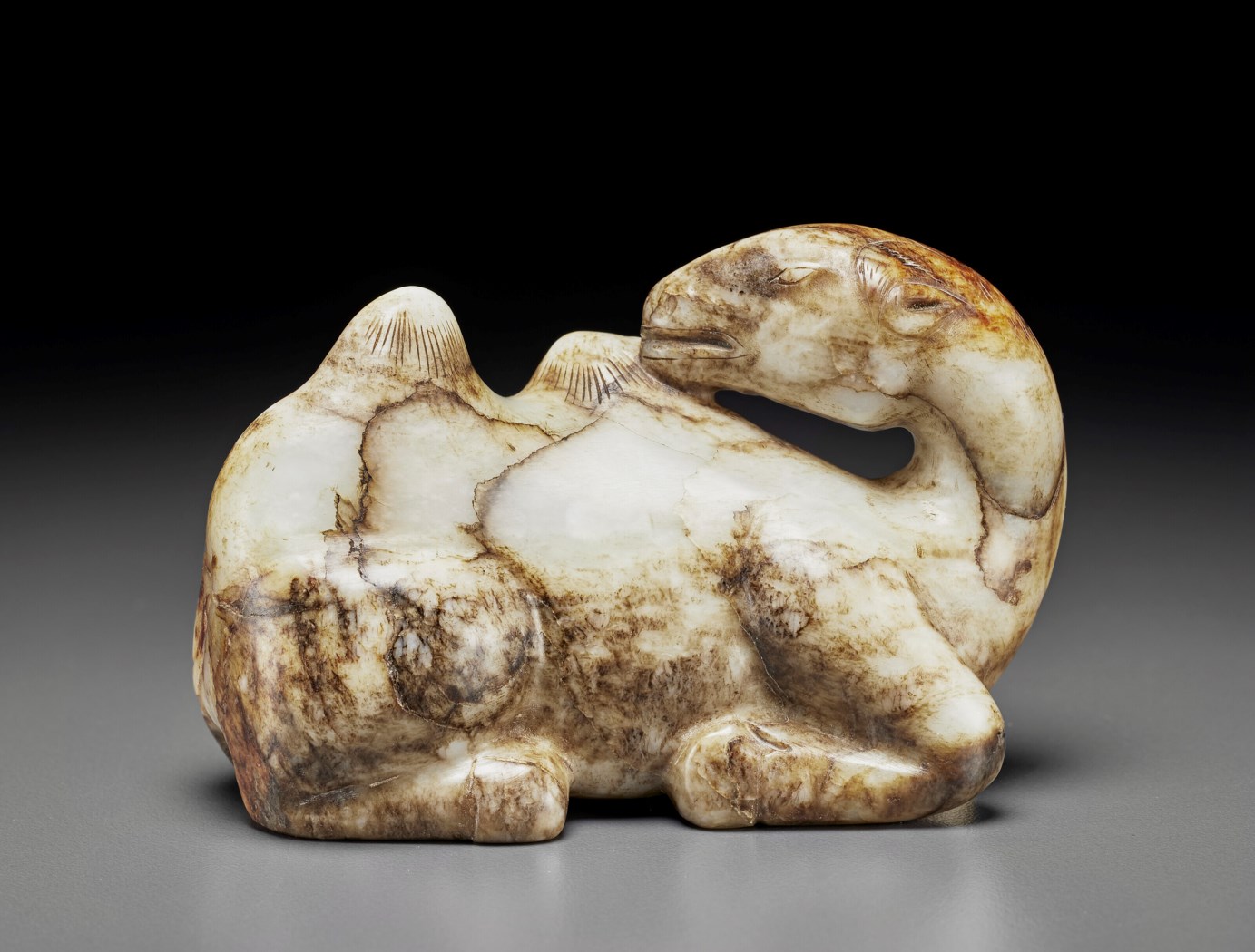 A MOTTLED GREY, BLACK AND RUSSET JADE FIGURE OF A RECUMBENT CAMEL ...